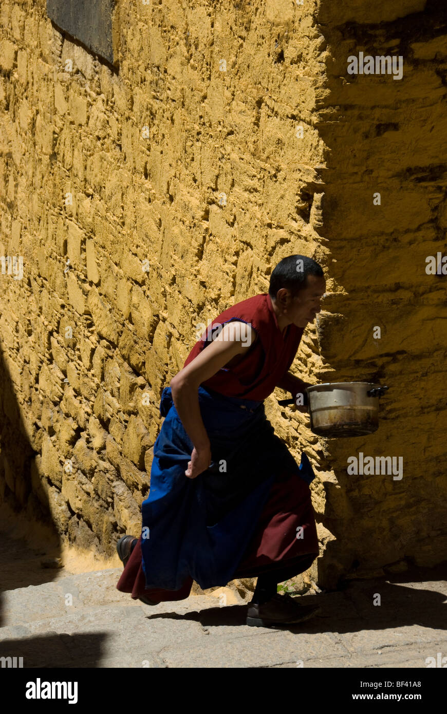 Tibetan Buddhist monk dressed in a red robe walking up steps beside the ...