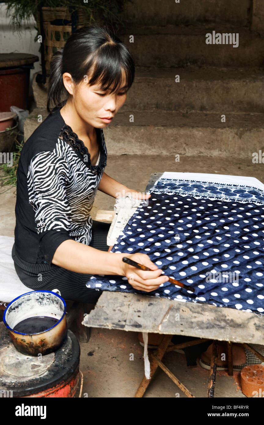 Miao woman drawing traditional pattern on white cotton cloth before wax ...