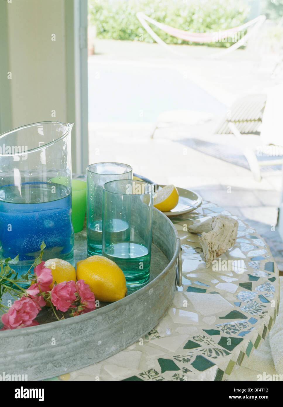Close-up of glass jug and glasses on circular metal tray on mosaic ...