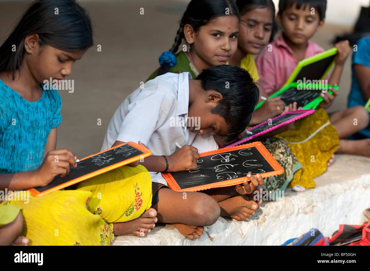 Indian school children sitting outside their school writing on ...