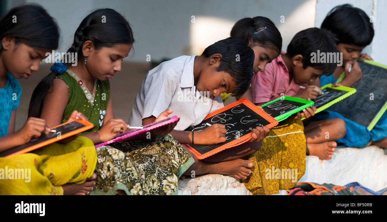 Indian school children sitting outside their school writing on ...