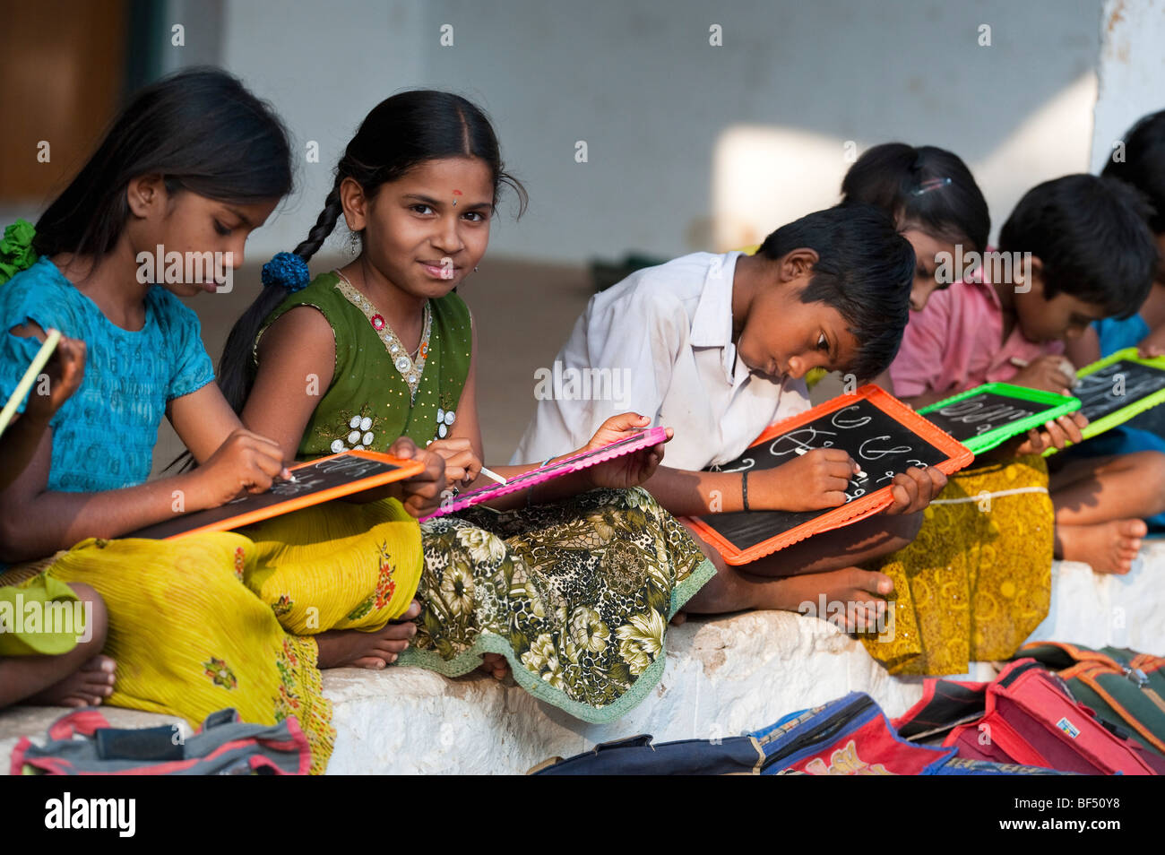 Indian school children sitting outside their school writing on ...