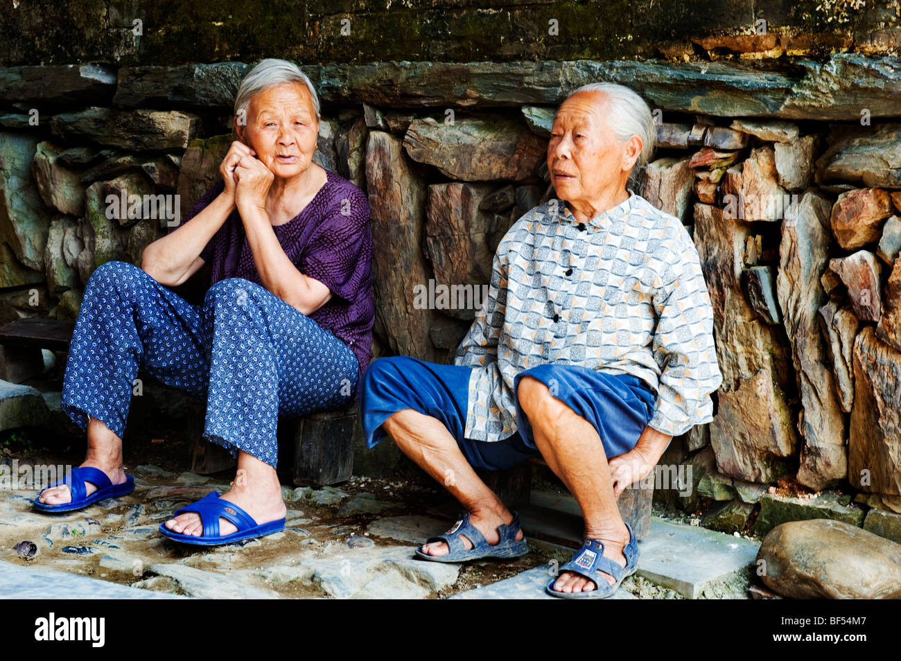 Two Dong elderly women sitting beside stone wall, Liping County ...