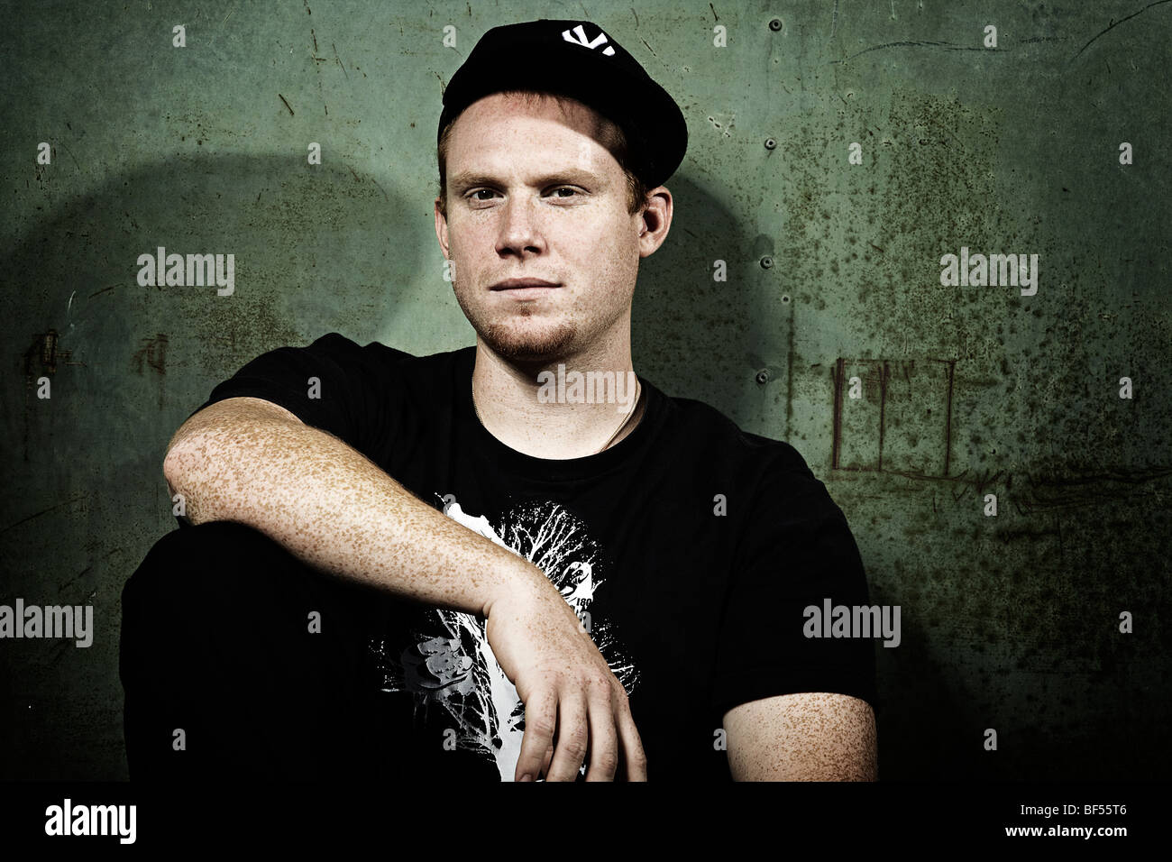 Portrait of a young man wearing a black cap sitting in front of a old ...