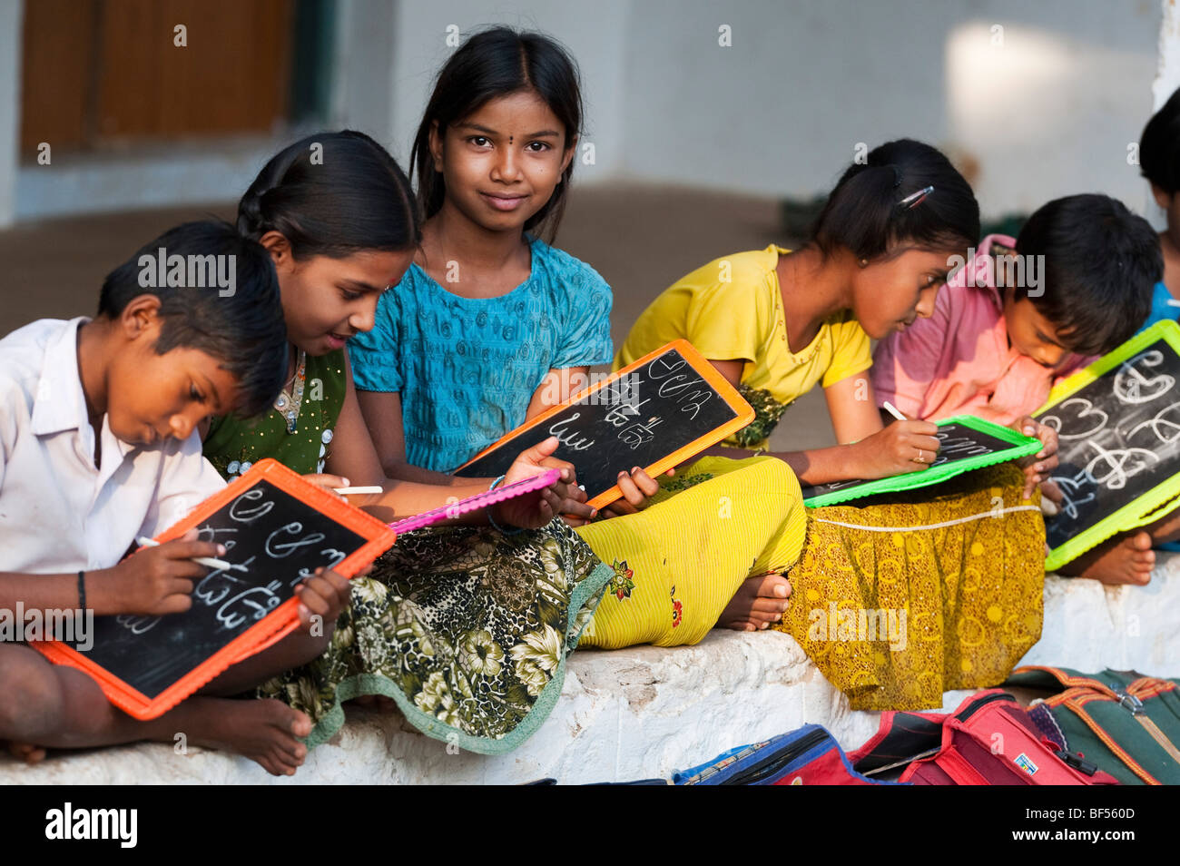 Indian school children sitting outside their school writing on ...