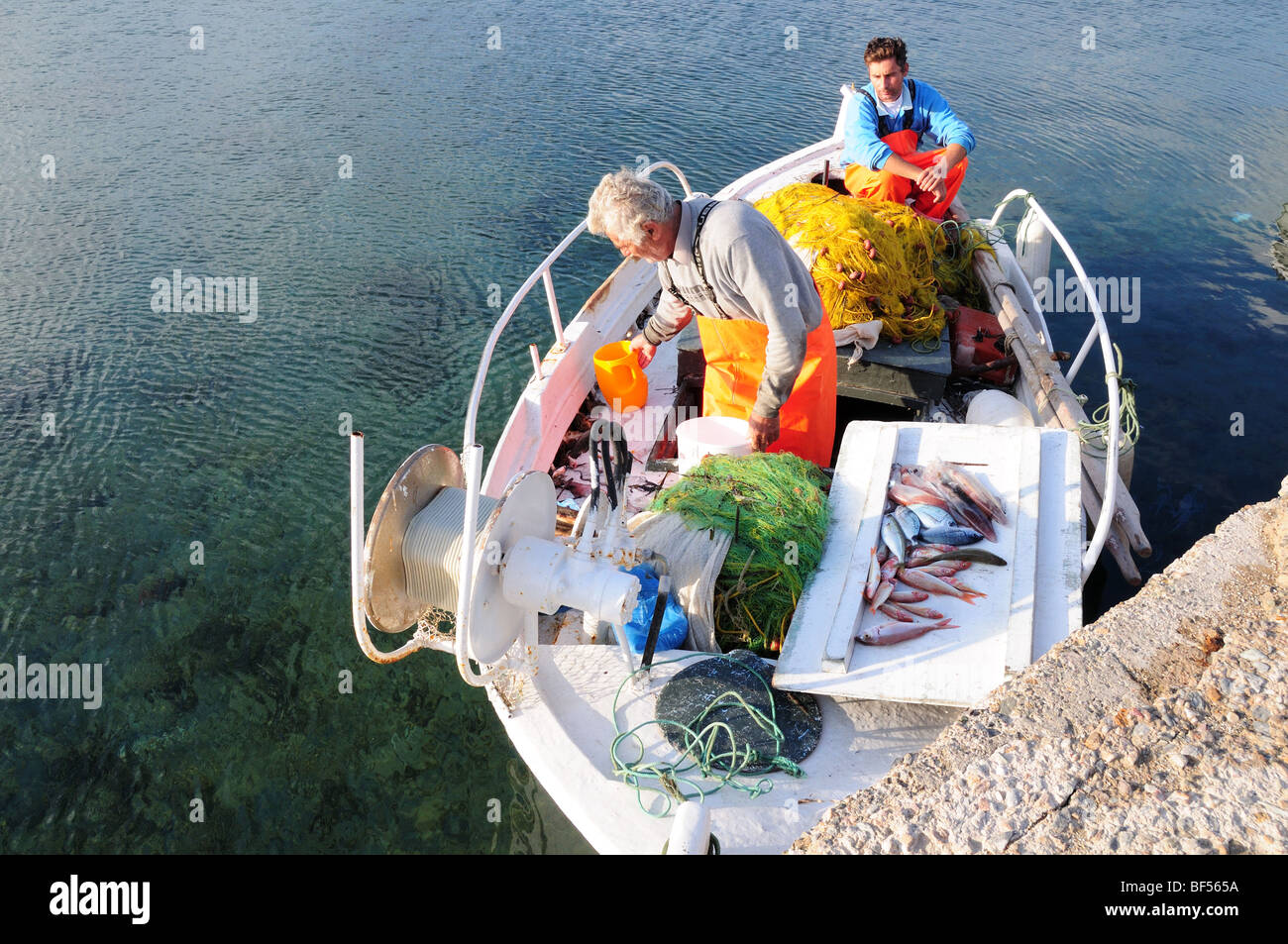 Two Greek fishermen in a small fishing boat with their catch of fish ...