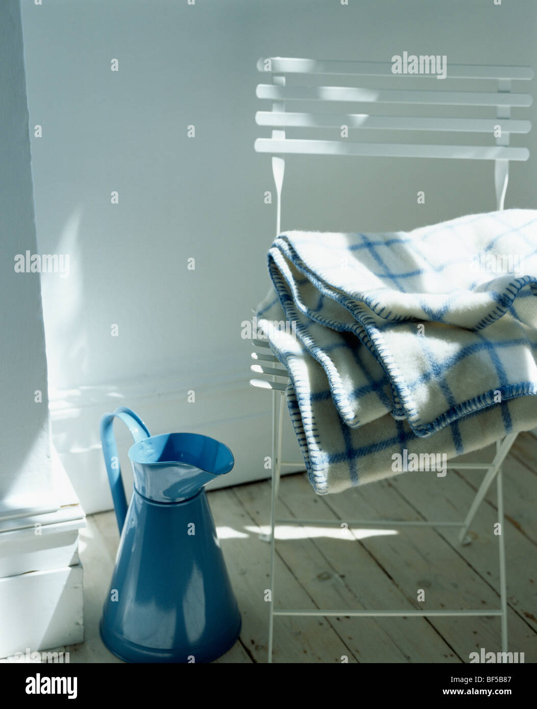 Close-up of old blue enamel jug beside white folding chair with blue ...