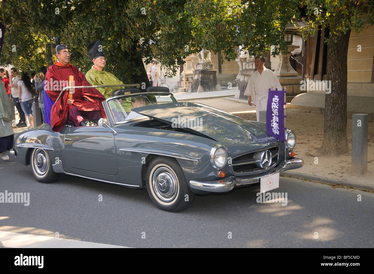 Priest being driven in a procession in a Mercedes with the hood raised ...