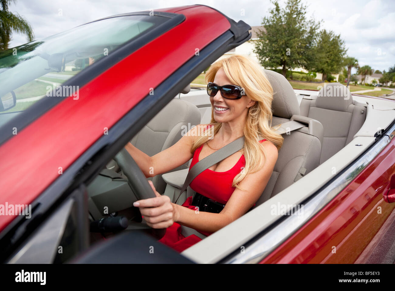 A beautiful young blond woman driving her convertible car wearing a red ...