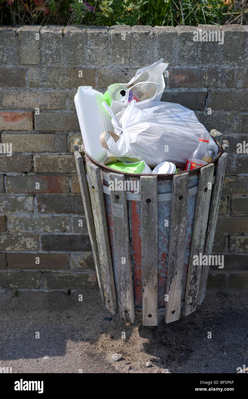 street rubbish bin overflowing with garbage attached to brick wall ...