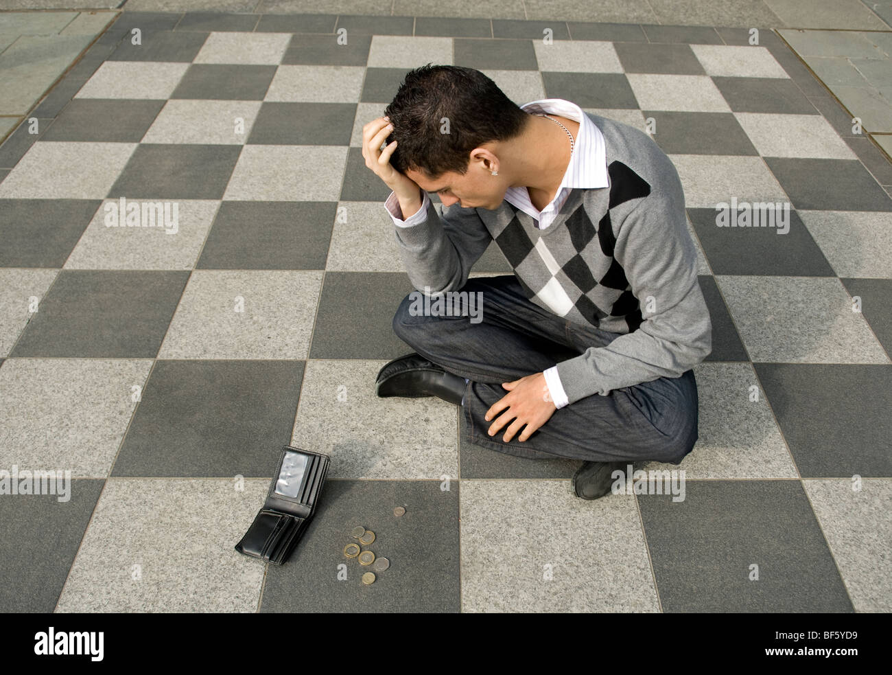 A young man with his wallet on chequered concrete floor, money spilling ...