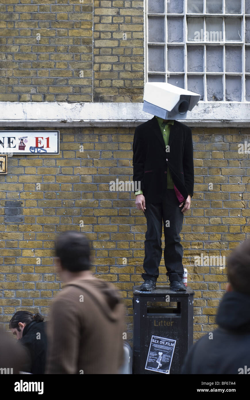 A man with a surveillance camera as a mask stands over the busy crowd ...