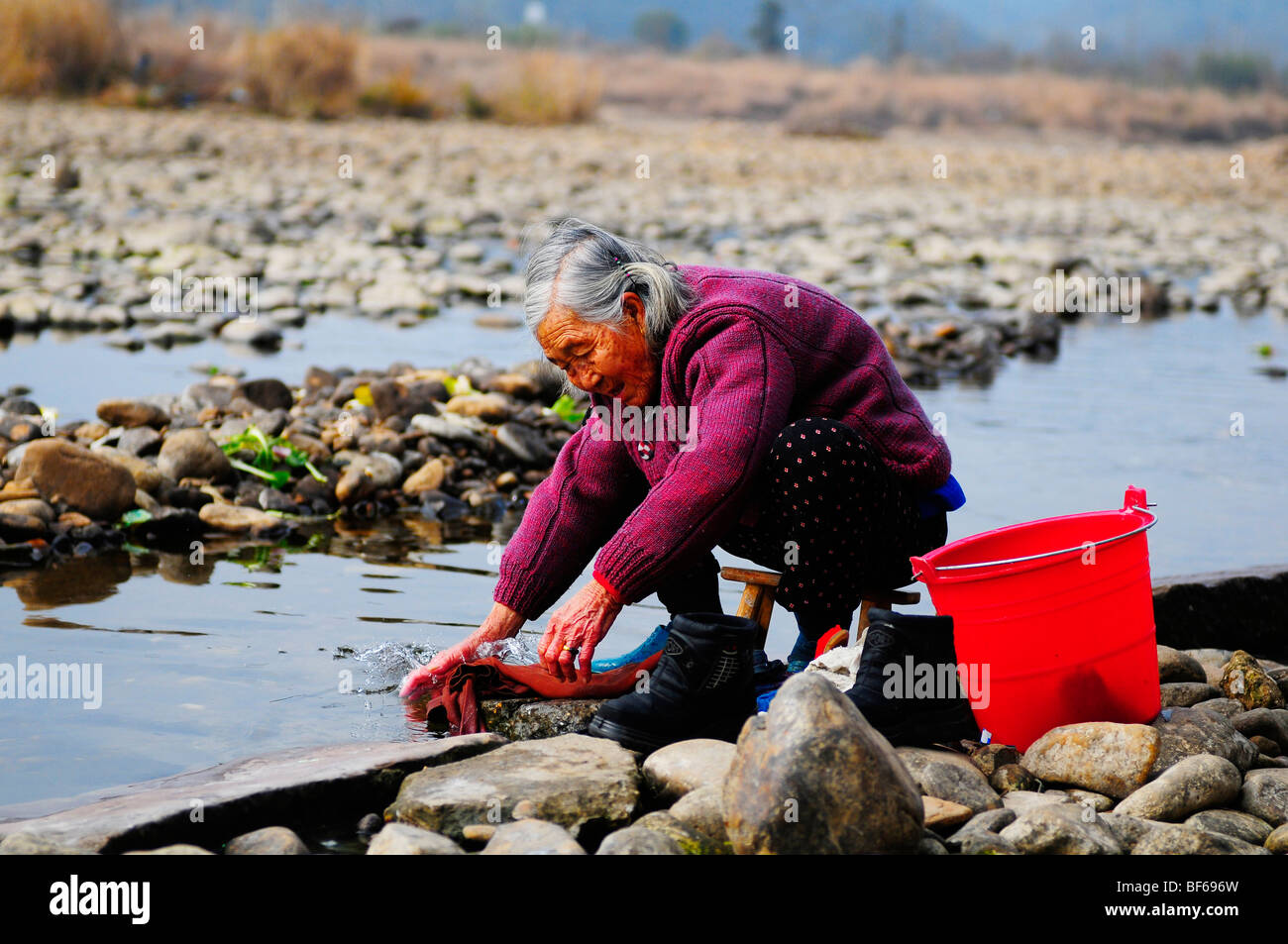 Elderly Chinese woman washing clothes beside creek, Shangqing Ancient ...