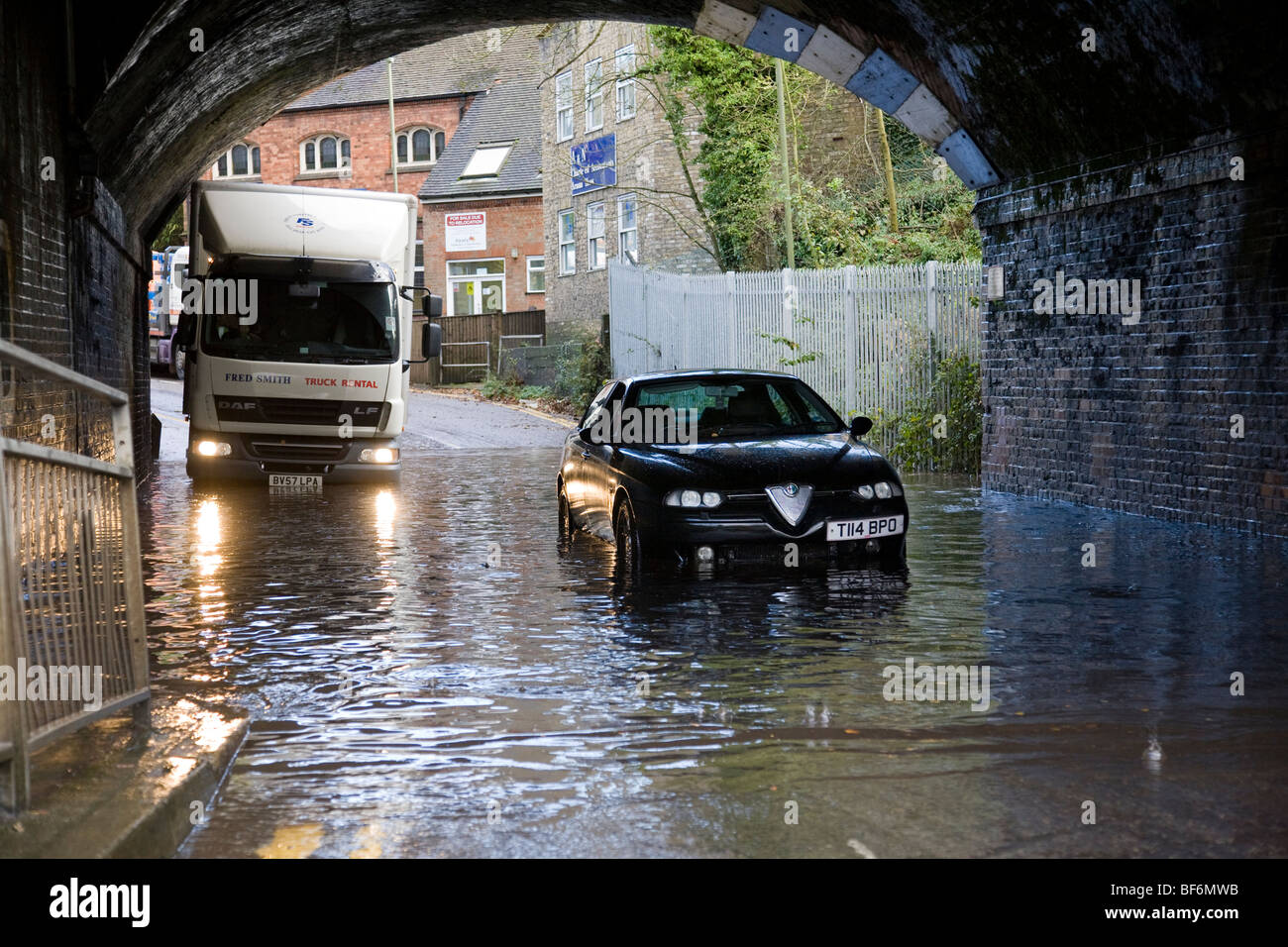 A lorry attempts to ease its way past a stranded car under a flooded ...