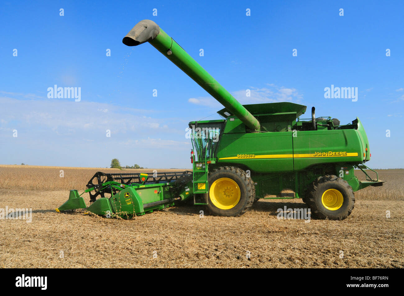 A John Deere green combine harvests soybeans on a Midwestern farm field ...