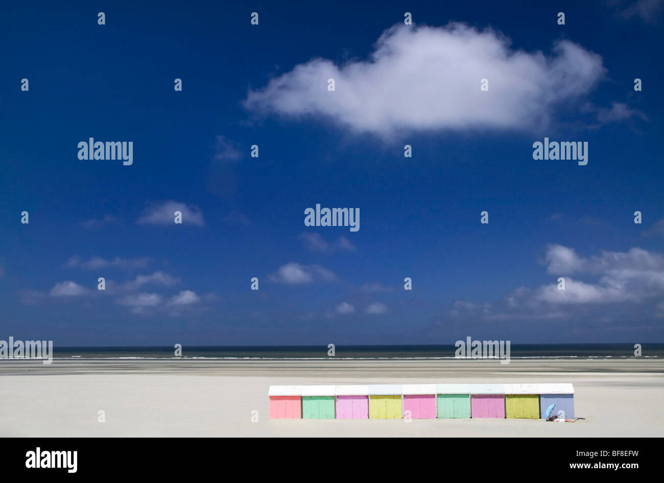 NORMANDY Pastel coloured beach huts sun umbrella and sunbathing couple ...