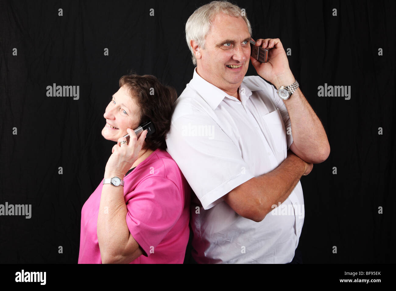 Mature late middle aged married couple standing back to back calling ...