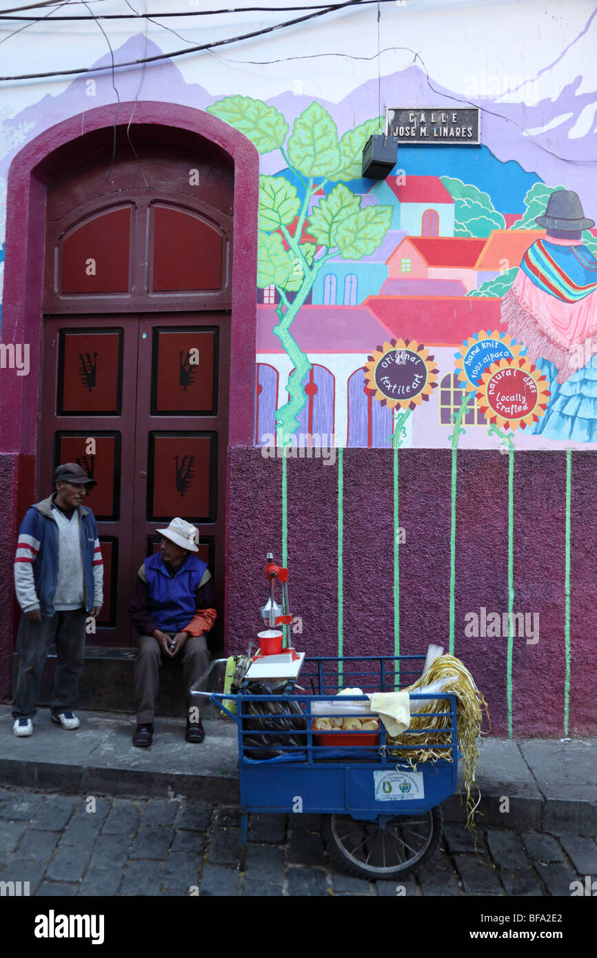 Man selling orange juice from cart in front of handicraft shop with ...