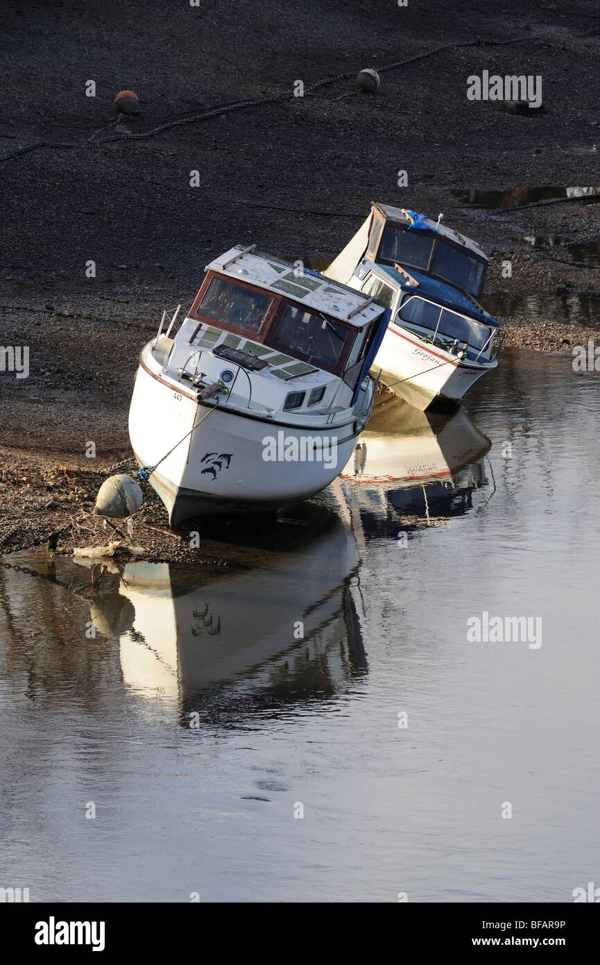Two boats cast reflections in the low tide water of the River Thames by ...