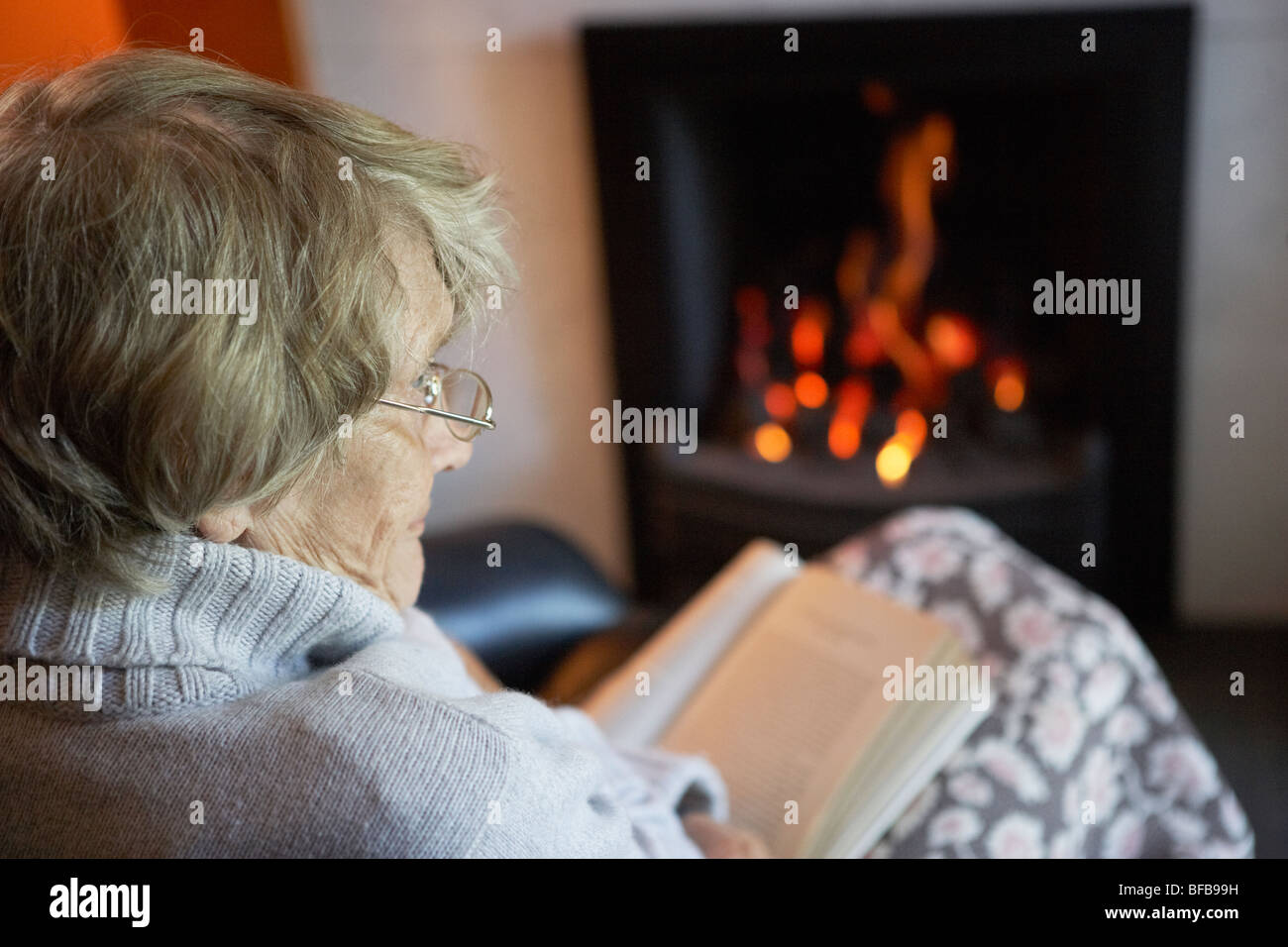 Senior Woman Reading Book By Fire At Home Stock Photo - Alamy