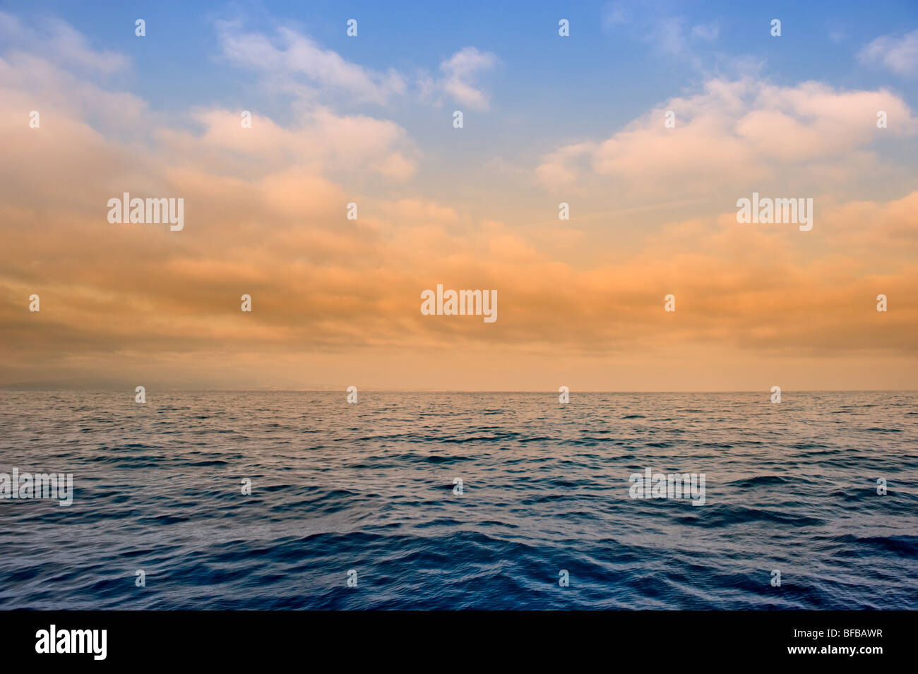 A low sun lit cloudscape scene over the oceans surface shows a moody ...
