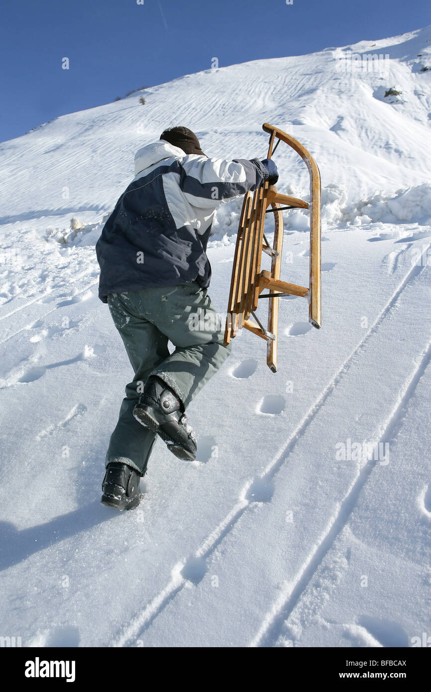 Man climbing a snowy hill with a wooden sled Stock Photo - Alamy