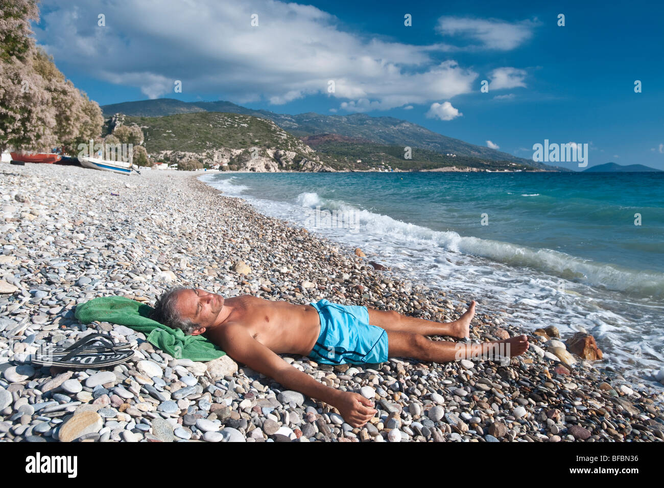 man sunbathing and relaxing on a beach near the blue sea with mountain ...