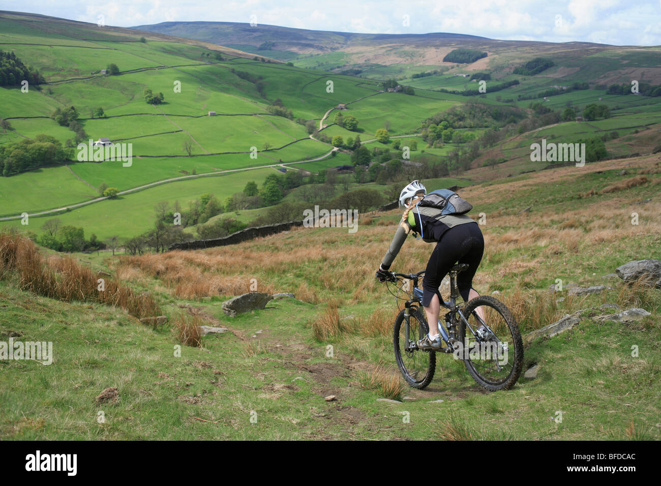 A woman mountain bides down a steep trail in the Yorkshire Dales area ...