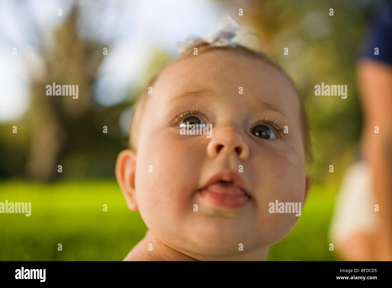 A wide-eyed, baby girl looks up with an open mouth while outside with ...