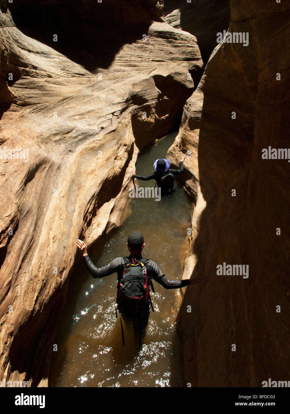 Two people wade through water while hiking down a slot canyon in Utah ...