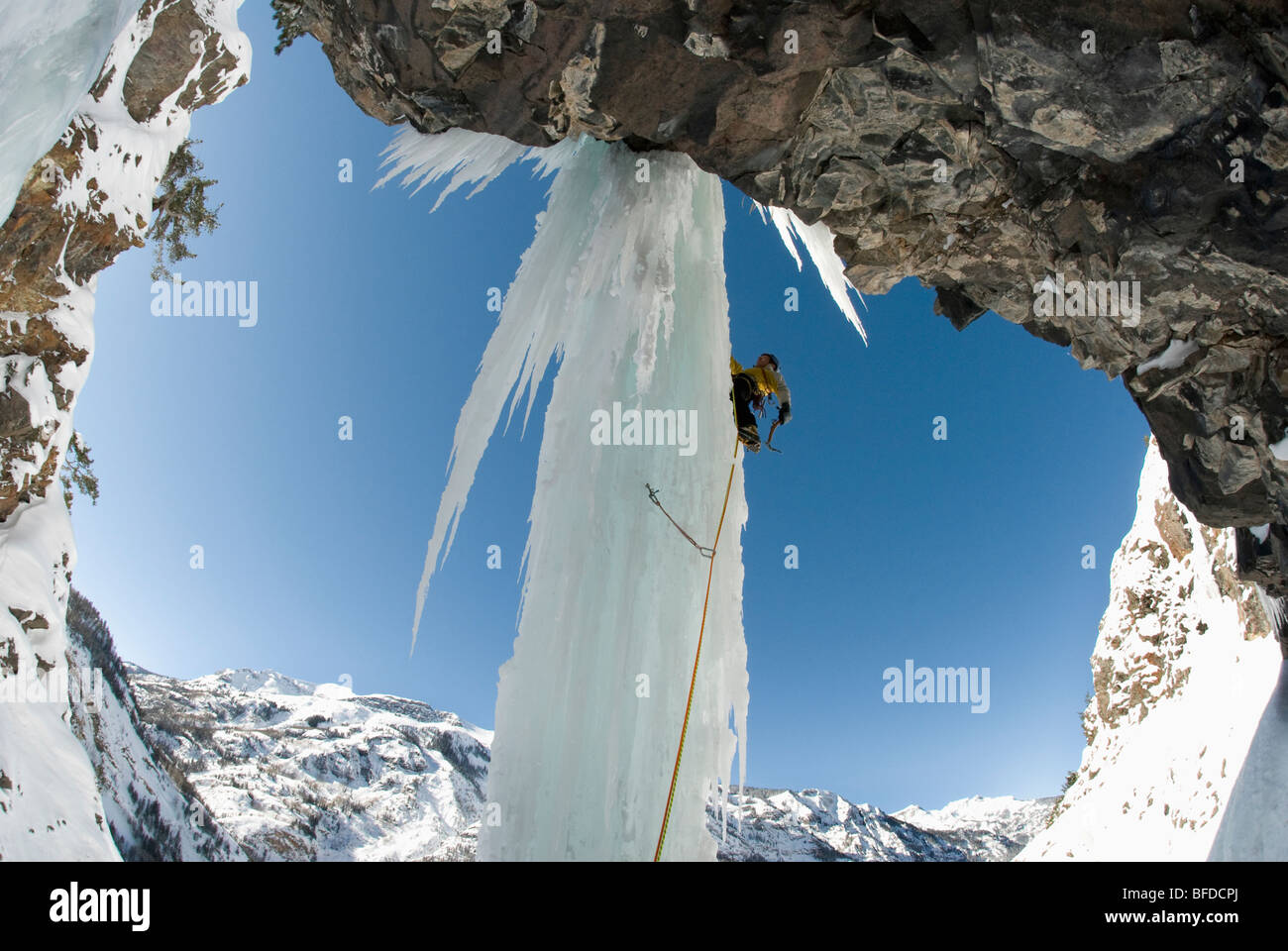 A professional male climber ascends a frozen waterfall pillar while ice ...