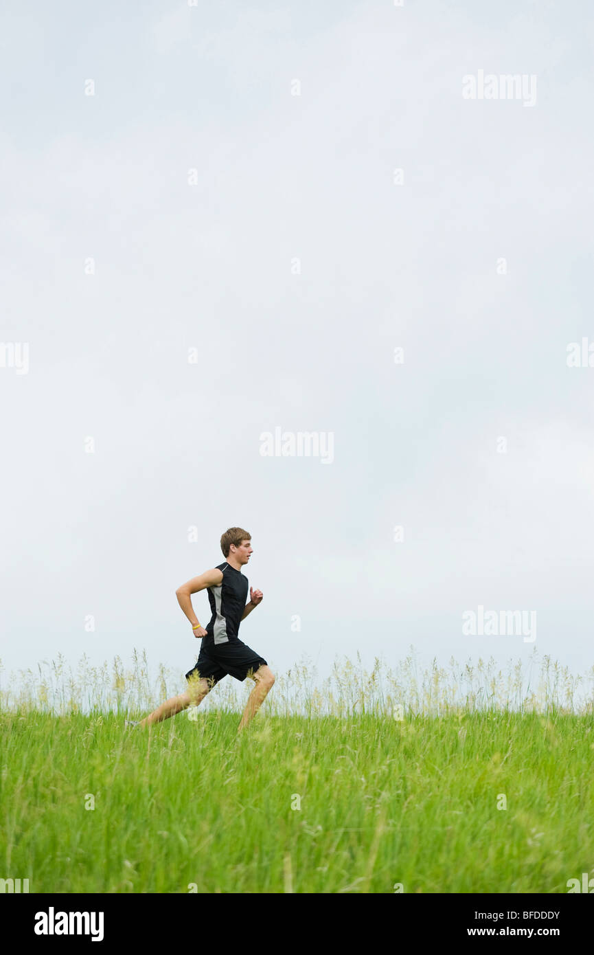 Young man running on a grass trail through a bright green field at ...