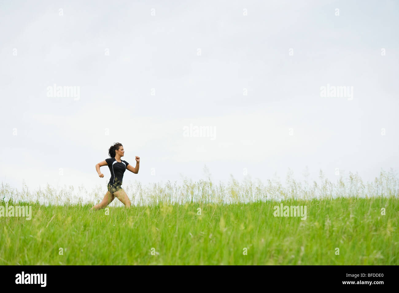 Young woman running on grass trail through a bright green field at ...