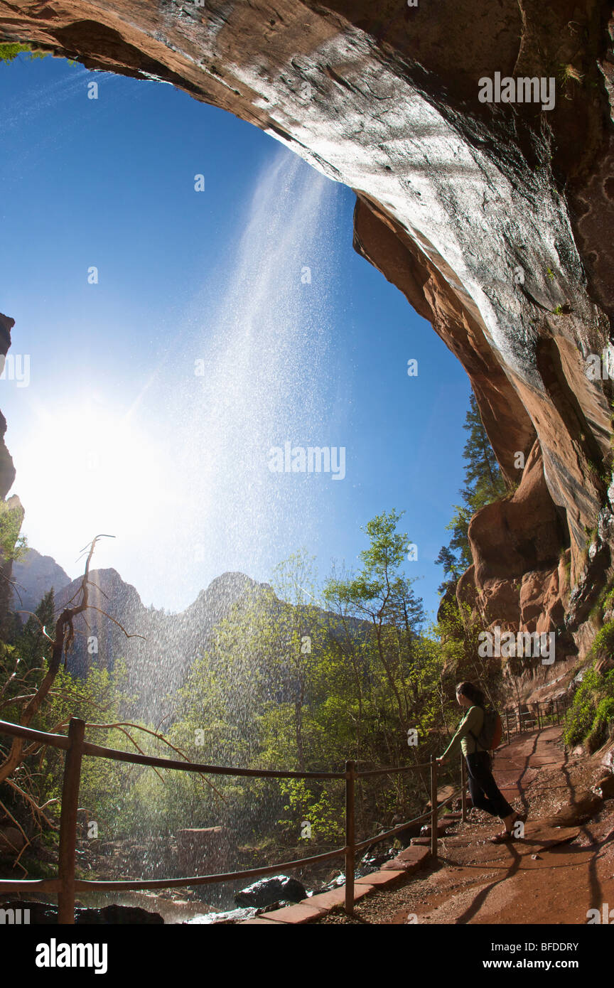 A hiker takes a break while walking under a waterfall in Zion National ...