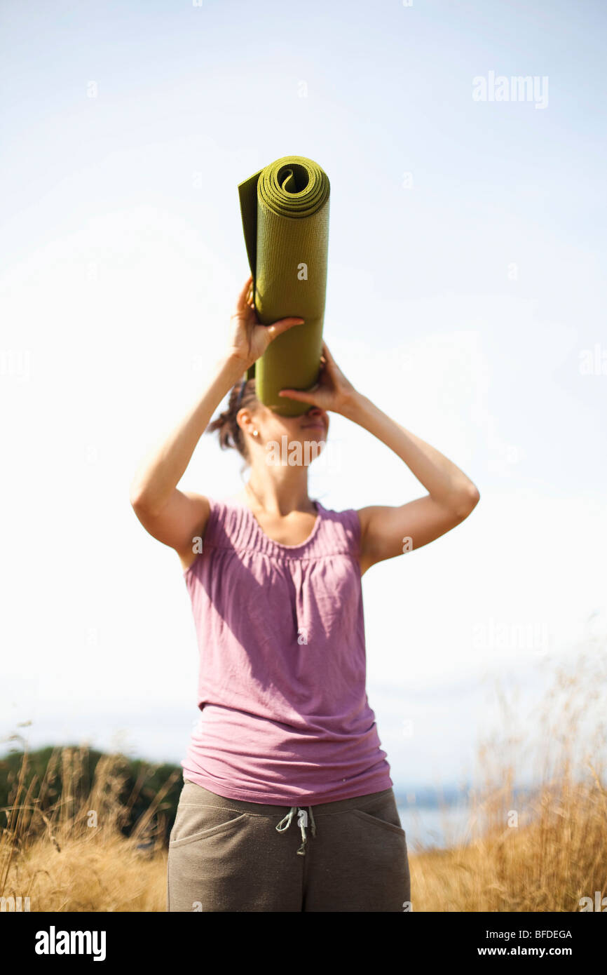 A young woman playfully looks through her yoga mat, acting like it is a ...