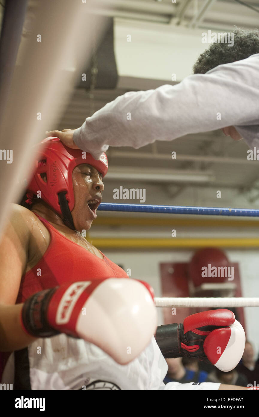 A female boxer catches her breadth while being coached between rounds ...