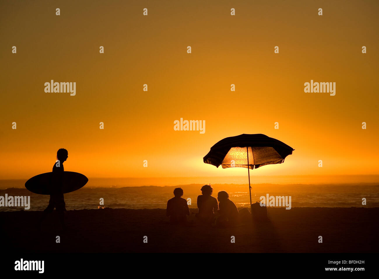 Beachgoers are silhouetted by the sunset on Camps Bay Beach in Cape ...
