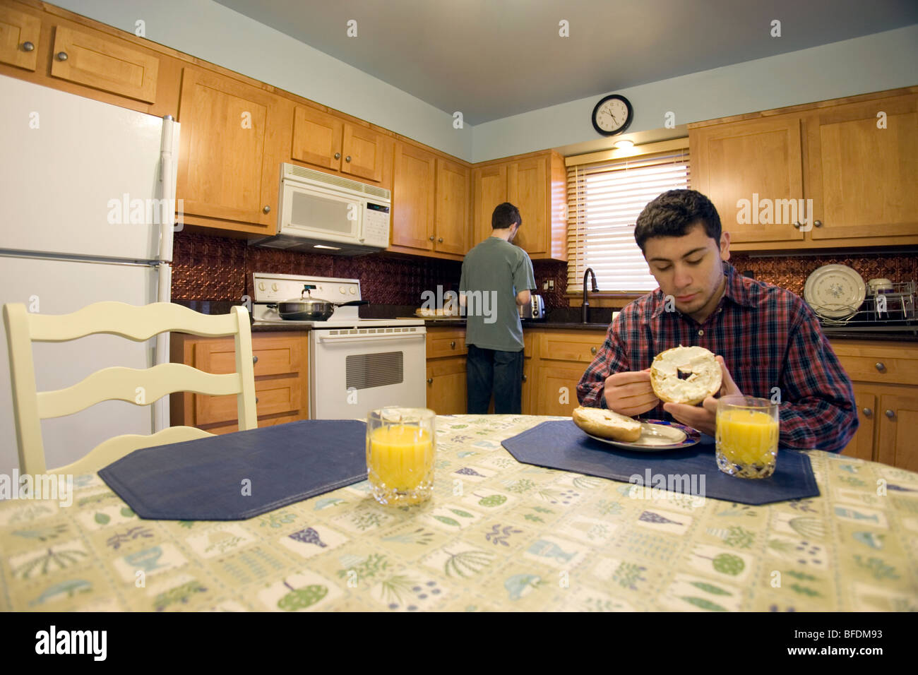 Two young men sits at a kitchen table ready for and eating breakfast ...