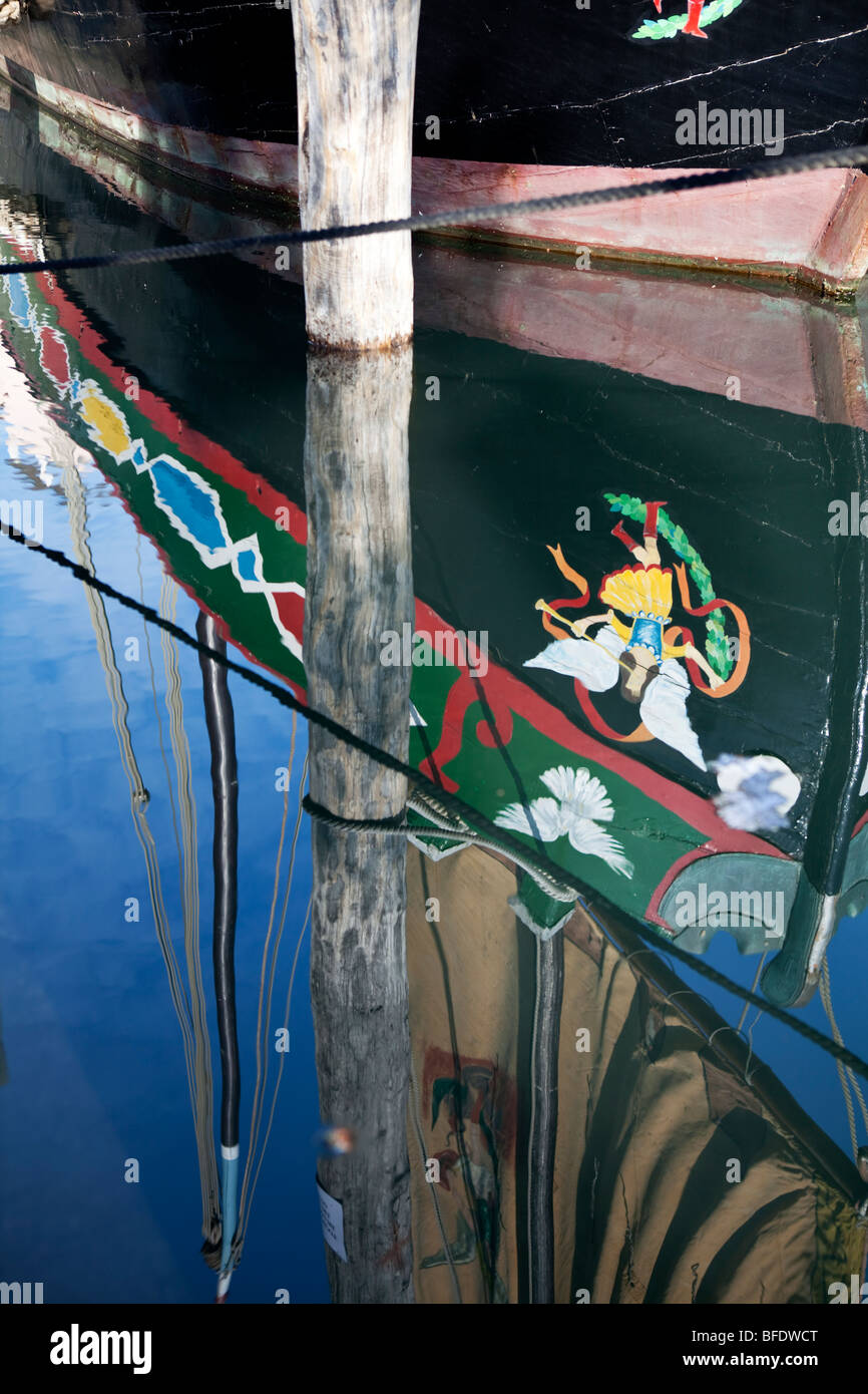 Antique wooden sailboat with painted angel on side reflected in the sea ...