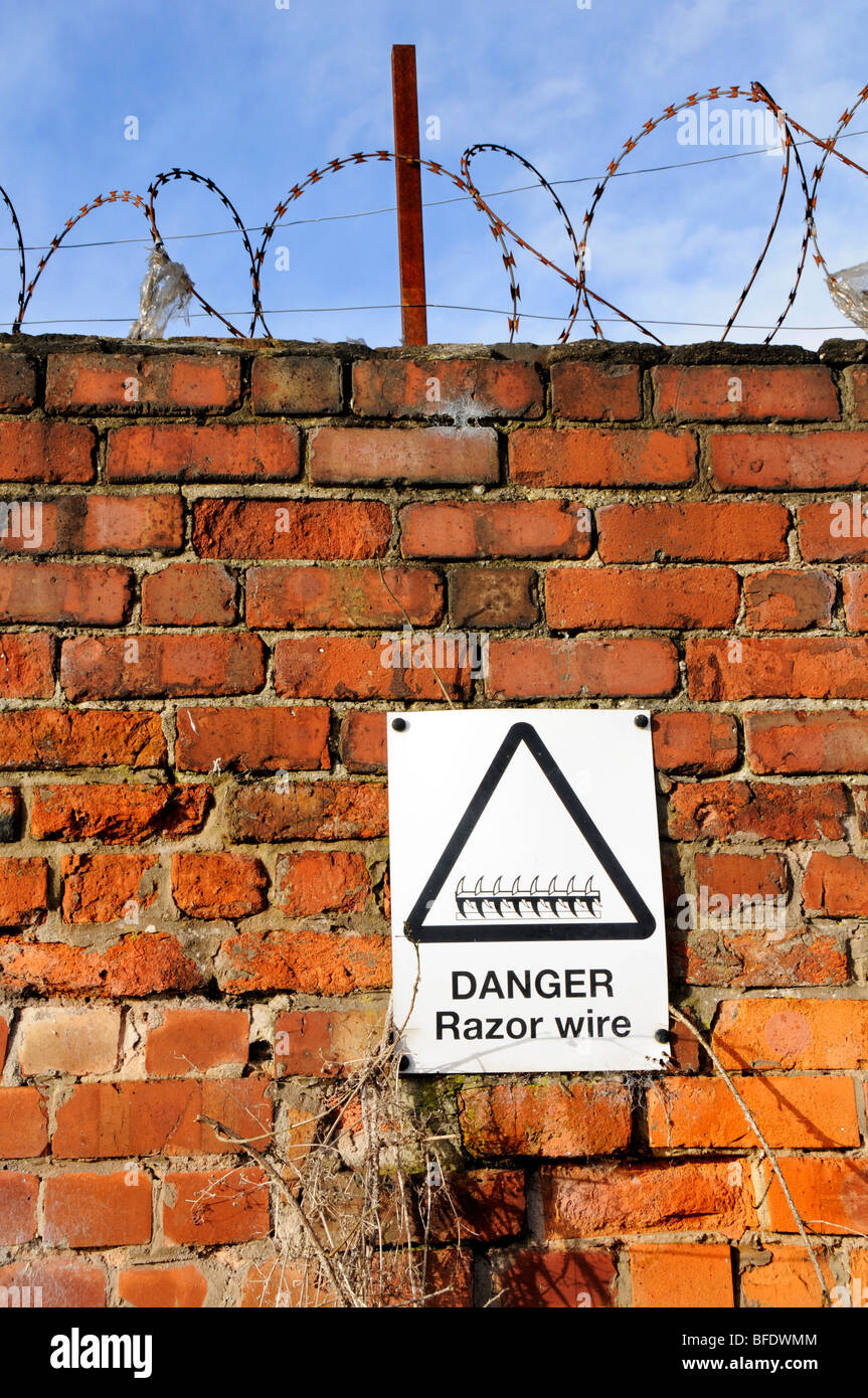 A danger sign on a brick wall warning of razor wire Stock Photo - Alamy
