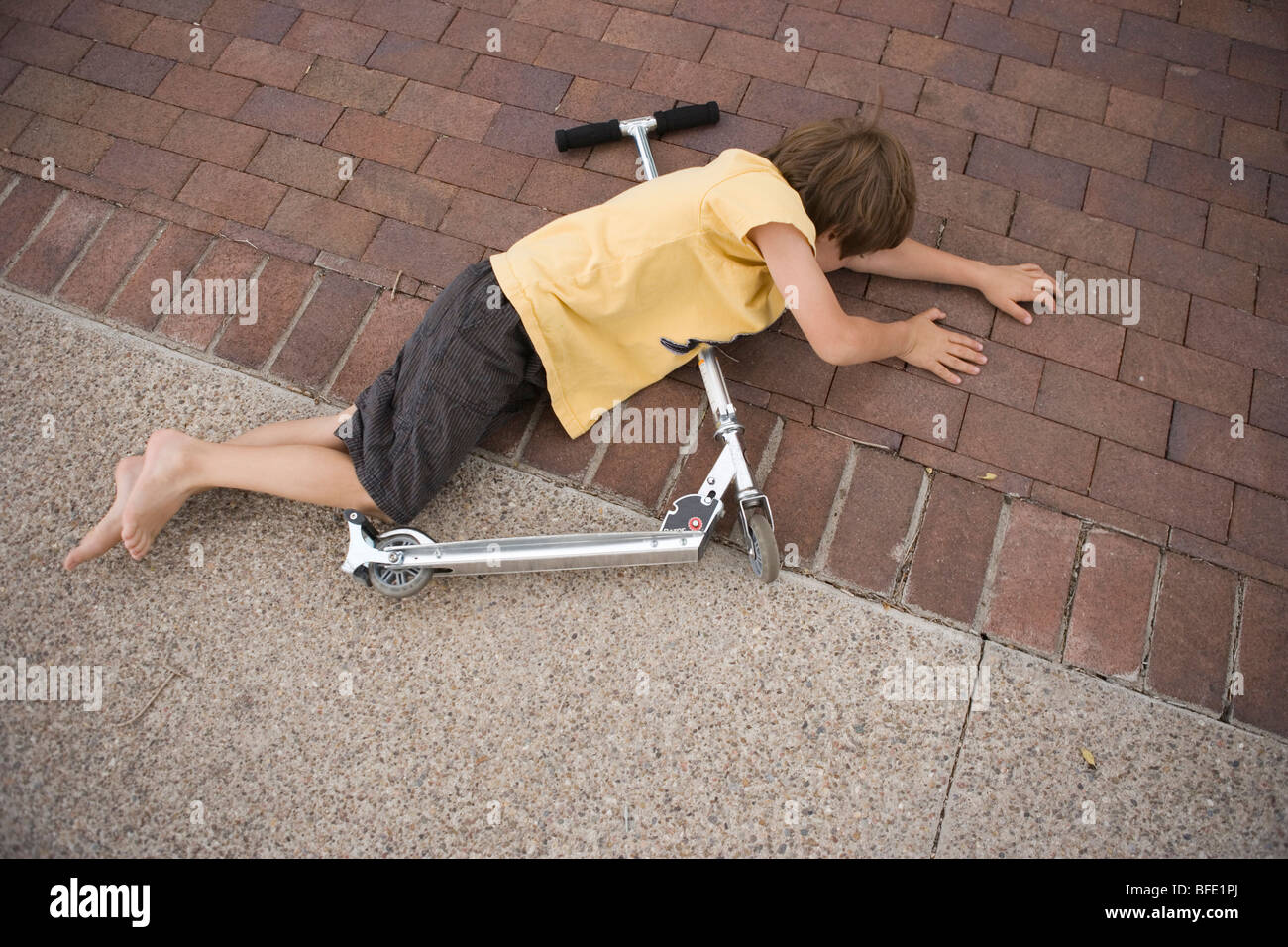 seven year old boy falls off his scooter and lands on the driveway ...
