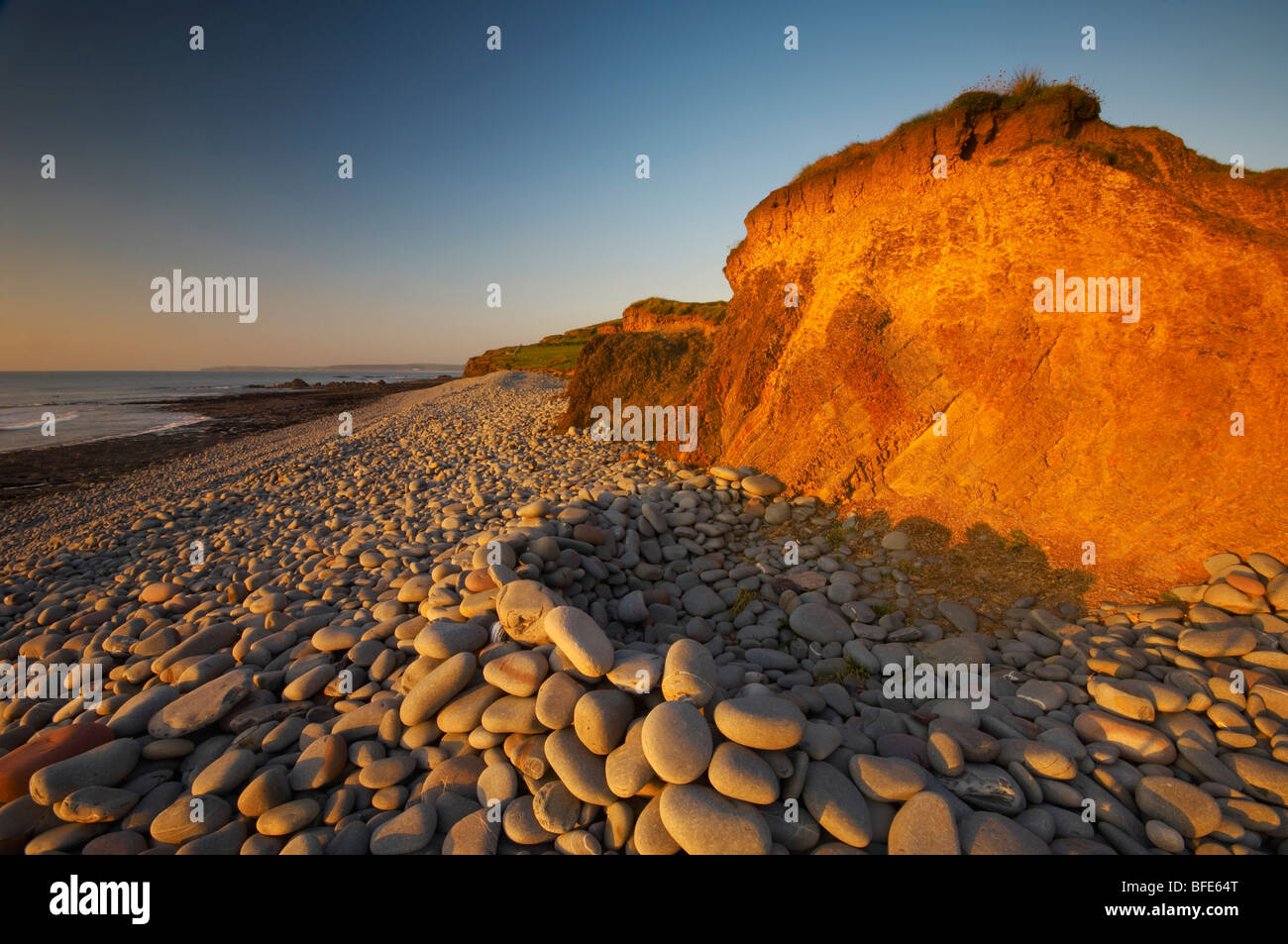 Late evening sunlight illuminates the orange cliffs at Abbotsham beach ...
