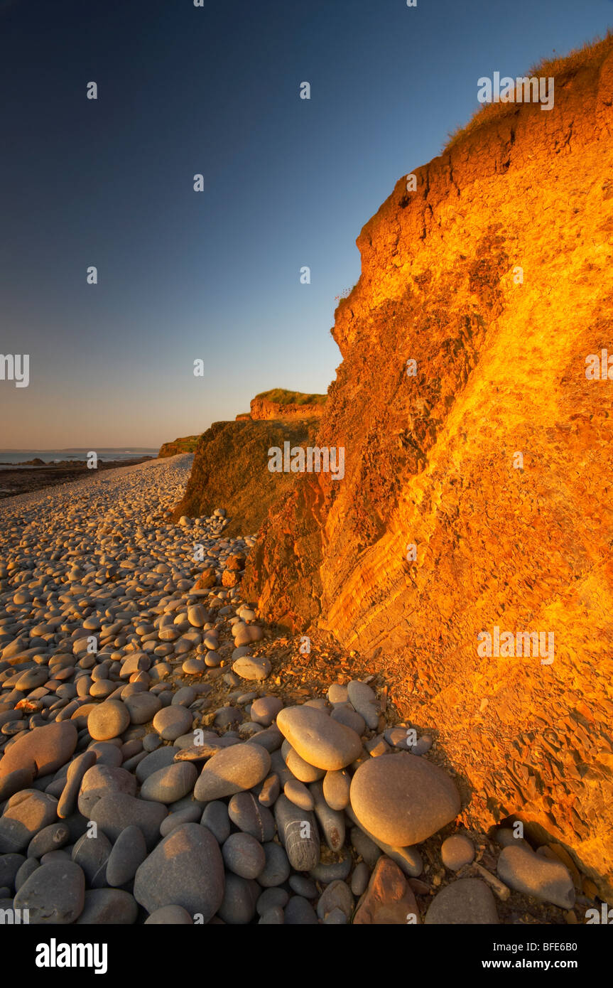 Late evening sunlight illuminates the orange cliffs at Abbotsham beach ...