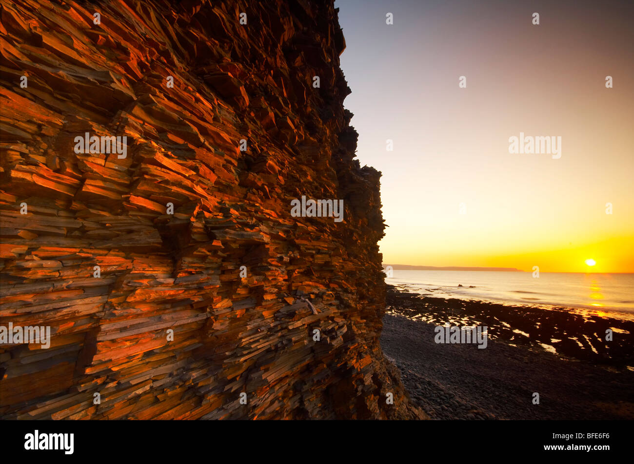 Late evening sunlight illuminates the orange cliffs at Abbotsham beach ...