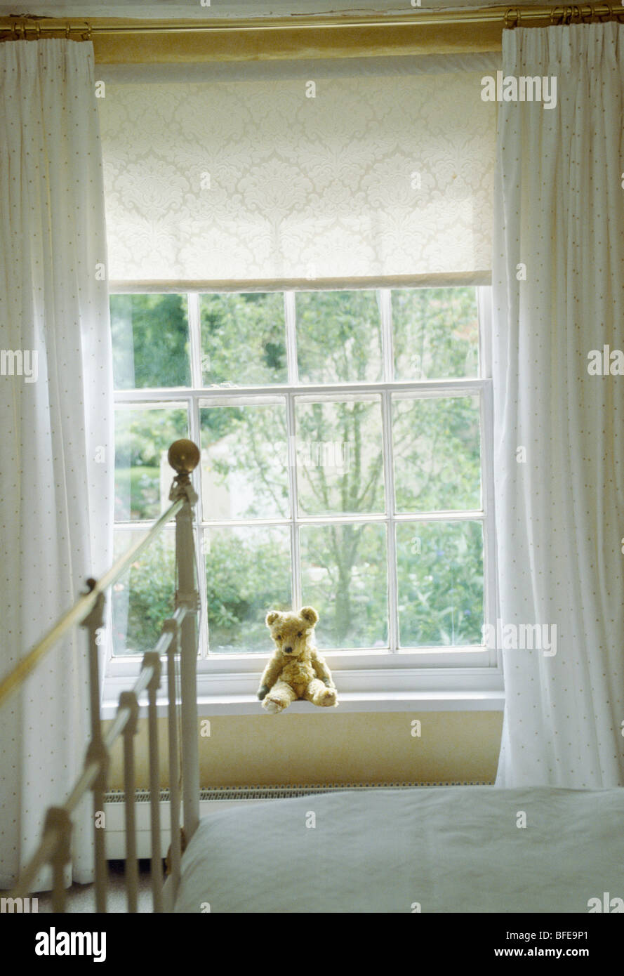 Teddy-bear on window-sill of window with cream lace blind and white ...