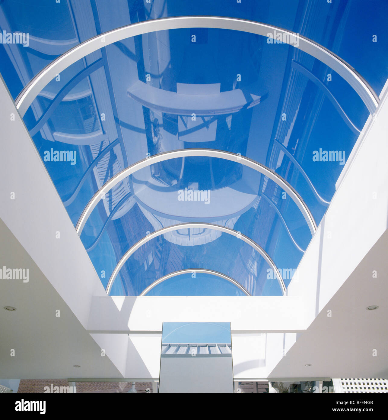 Looking up at blue sky through curved glass ceiling of modern hall ...