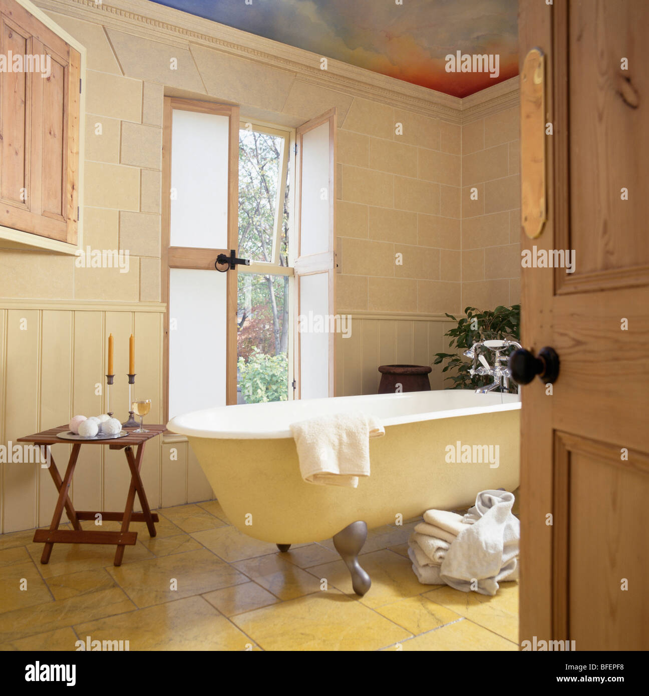 Roll-op bath in front of open French windows with opaque glass in cream ...