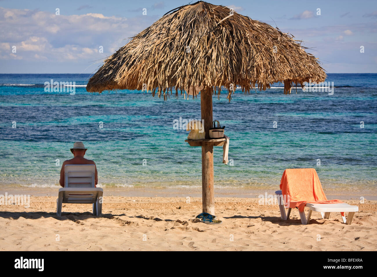 Beach scene: man sitting on sandy beach in palm umbrella shade; coral ...