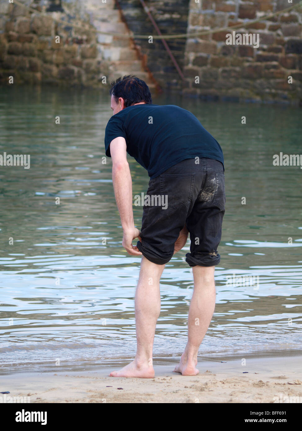 Man rolling up trouser legs to go paddling Stock Photo - Alamy
