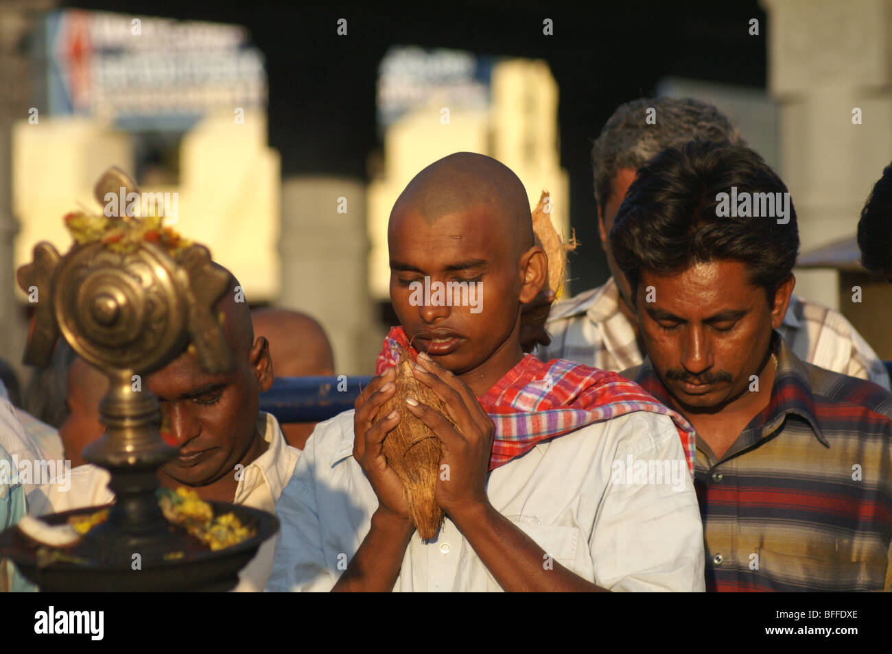 Shaven headed Hindu pilgrim praying with coconut at the Tirumala ...